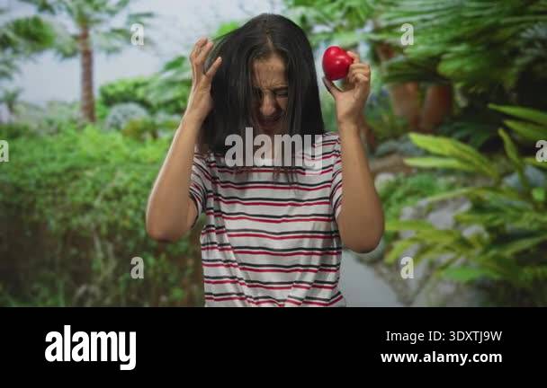 Woman holding a red heart and pressing hand to head on a forest path ...