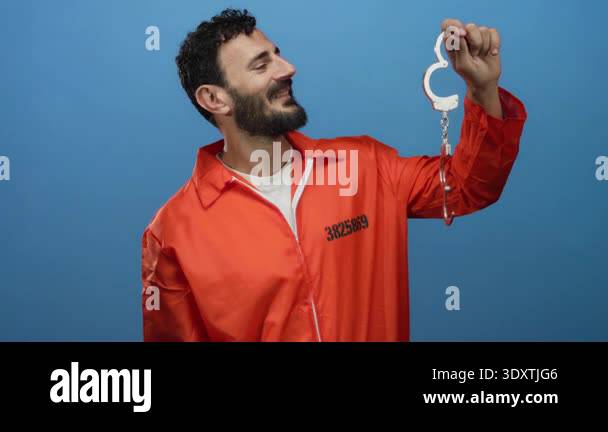 Hispanic man with beard in orange prison jumpsuit holding handcuffs ...