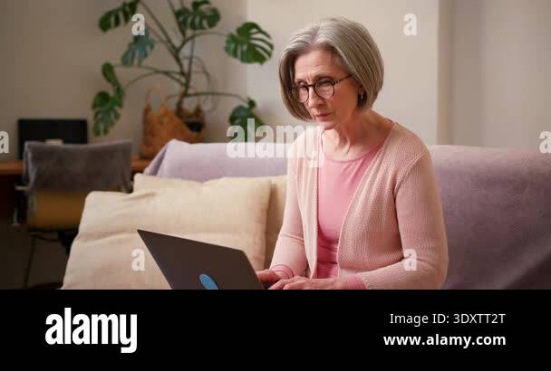 Mature old 60s woman student working at home using laptop technology ...