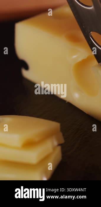 Someone cuts slices of cheese in a kitchen. The person uses a knife to ...