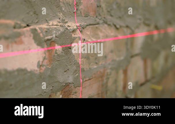 Close up of builder marking brick wall with pencil using red laser ...