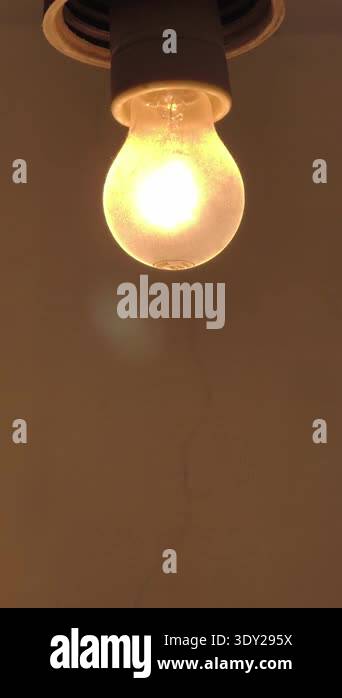 Frosted incandescent light bulb glowing with warm yellow light while ...