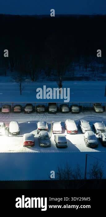 Snow-covered cars rest in a night parking lot as accelerated light ...