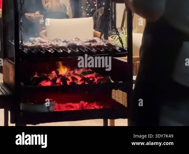 Elderly man raising grill to lower heat, salting juicy meat cuts on ...