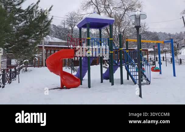 Colorful childrens playground with a slide and swings covered in snow ...