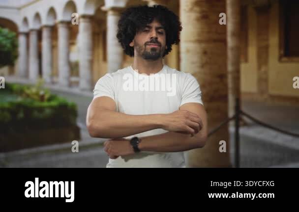 Man with crossed arms showing forearms and curly hair wearing white t ...