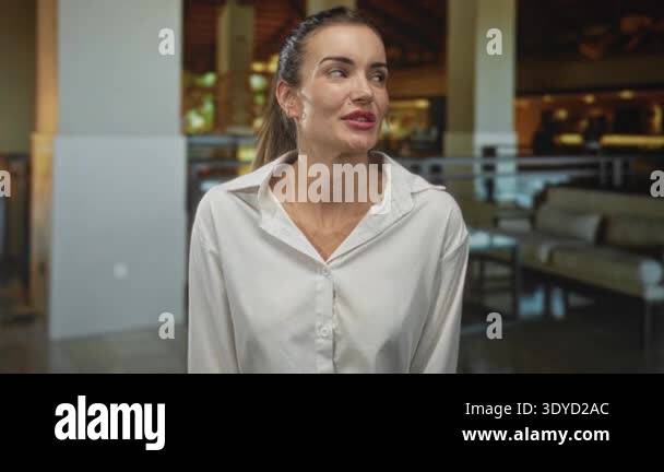 Woman shrugging shoulders with palms up in casual white shirt inside ...