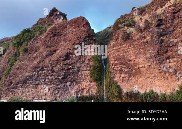 Observe a beautiful waterfall descending a rugged reddish-brown cliff ...