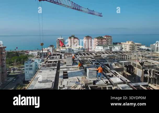 Aerial footage of active construction zone: tower crane moves materials ...