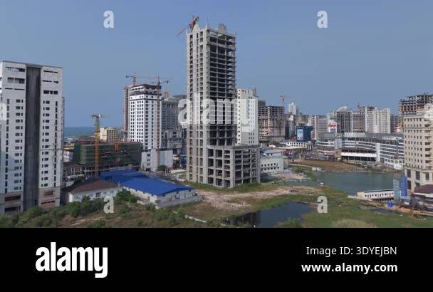 Backward aerial high-rise shells under construction, cranes, and pond ...