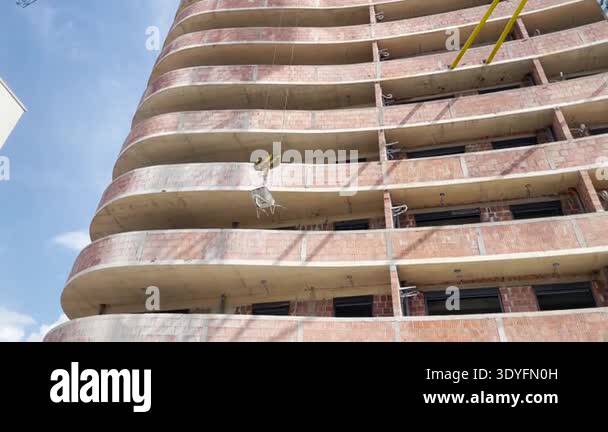 Construction crane lowers from upper floor to lower wheelbarrow with ...