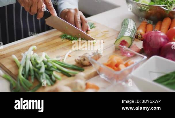 Home cook placing herbs on cutting board and chopping herbs with ...