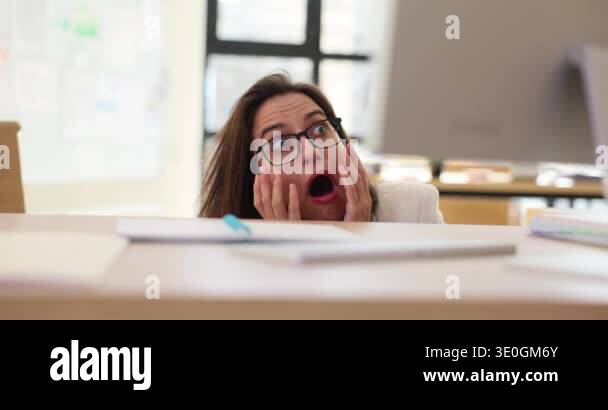 Shocked woman under table and looking at computer screen with eyes in ...