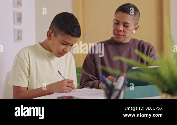 Latin mother tutoring her teenage son with his homework. The student is ...