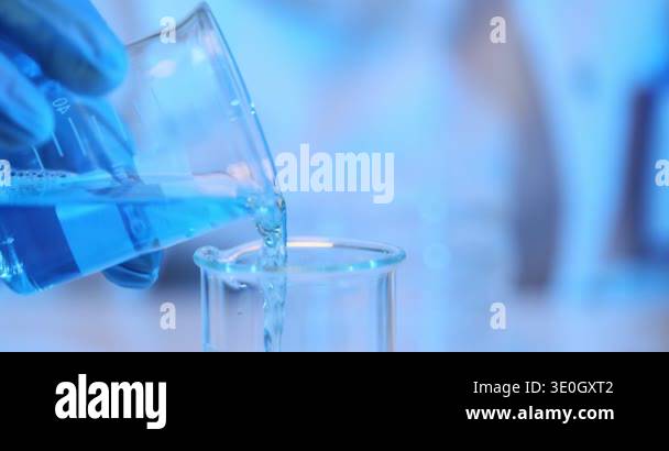 Blue liquid is poured from a glass beaker into a flask. Pouring a ...