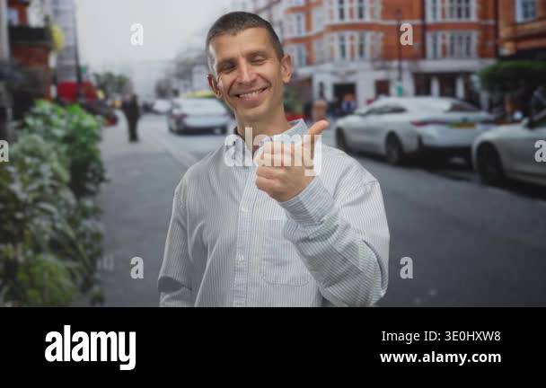 Man smiling on busy street giving thumbs up with a wink, conveying ...