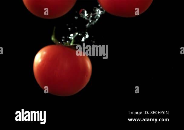 Fresh tomatoes falling under water on a black background. Filmed on a ...