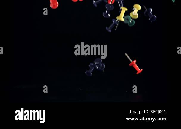 Multi-colored paper clips fall on a black background. Filmed on a high ...