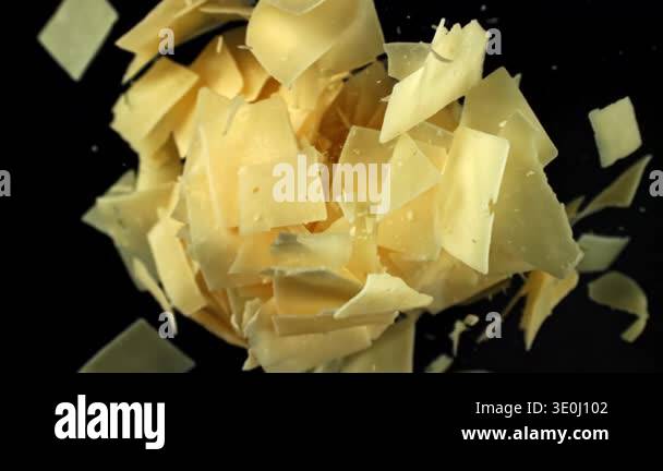 Parmesan cheese flakes fly upwards on a black background. Filmed on a ...