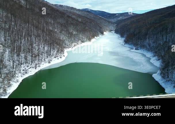 Aerial drone view of a partially frozen mountain lake surrounded by ...
