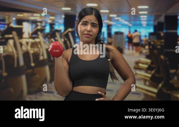 Woman holds red dumbbell at shoulder and shrugs shoulder in a gym ...