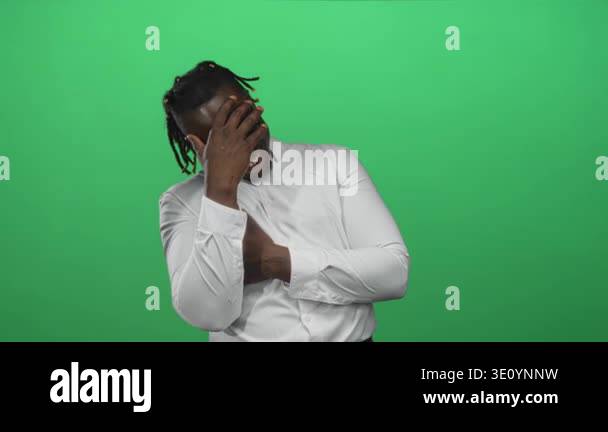 Man with hand covering face laughing in studio with green backdrop ...