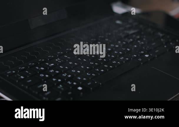 Angled view of a male hand wiping a black laptop keyboard surface with ...