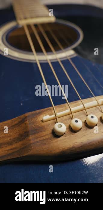Strings of a blue acoustic guitar stretched over the wooden bridge and ...