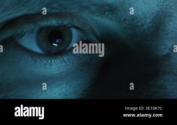 A dramatic close-up of a man's intense eyes staring at a monitor in a ...