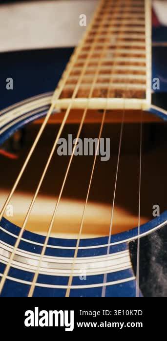 Golden strings on a blue acoustic guitar stretch over the soundhole and ...