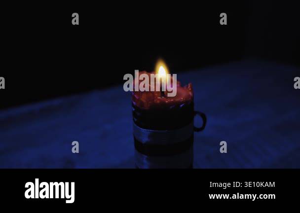 A hand uses a lit match to ignite the wick of a red candle in a dark ...