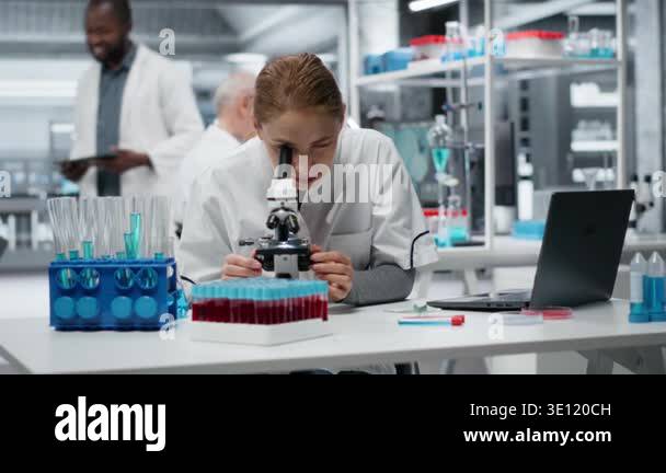 Clinical microbiologist using compound microscope for detailed cellular ...