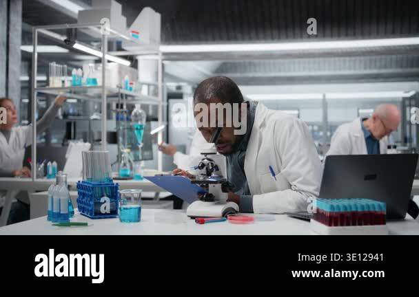 Male cytotechnologist using optical microscope to study microorganisms ...