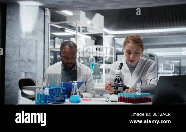 Pathologist examining biopsy slide while colleague documents diagnostic ...
