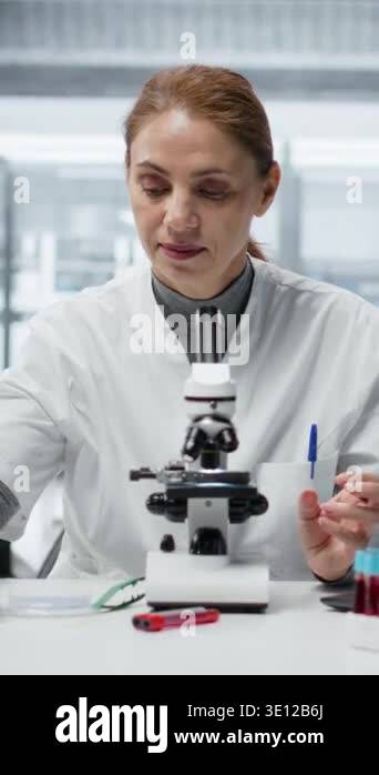 Vertical video Histology technician in lab inspecting thin glass slide ...