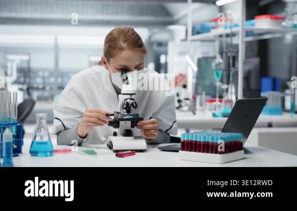 Technician wearing surgical mask examining pathology slides under ...