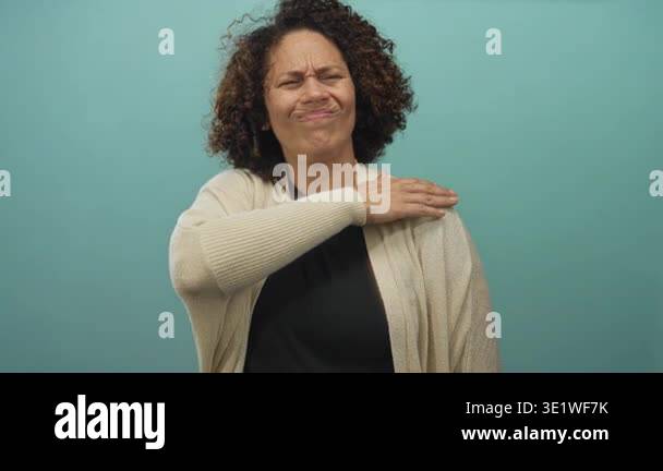 Hispanic woman clutching her left shoulder with a wince in pain against ...