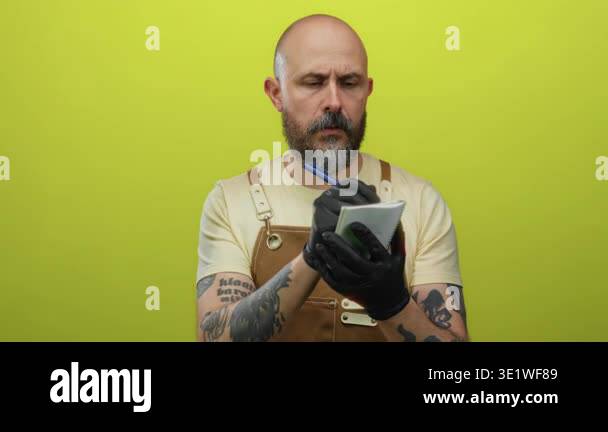 Bald man with tattoos writes notes in a small notebook on a vibrant ...