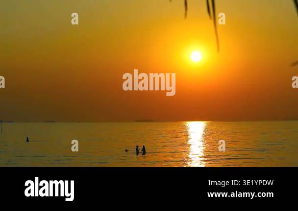 Serene Sunset Over Calm Ocean with Silhouetted Figures in Water Stock ...