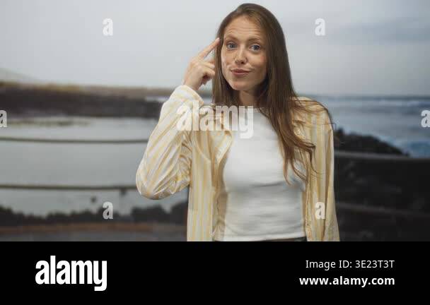 Woman shrugging with palm up by a seaside railing on the coast, eyes ...