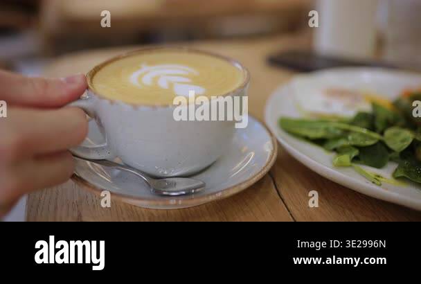 Person drinking delicious cup of flat white coffee near plate of ...
