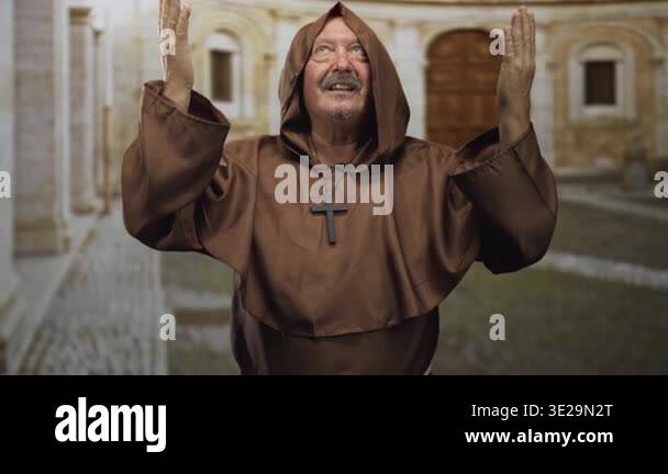 Man monk in brown habit with visible hands raised in prayer and cross ...
