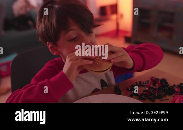 Candid indoor scene of child gripping burger with sesame bun and ...