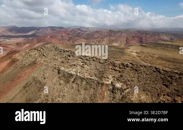 Rocky desert plateau overlooking layered red and brown mountains under ...
