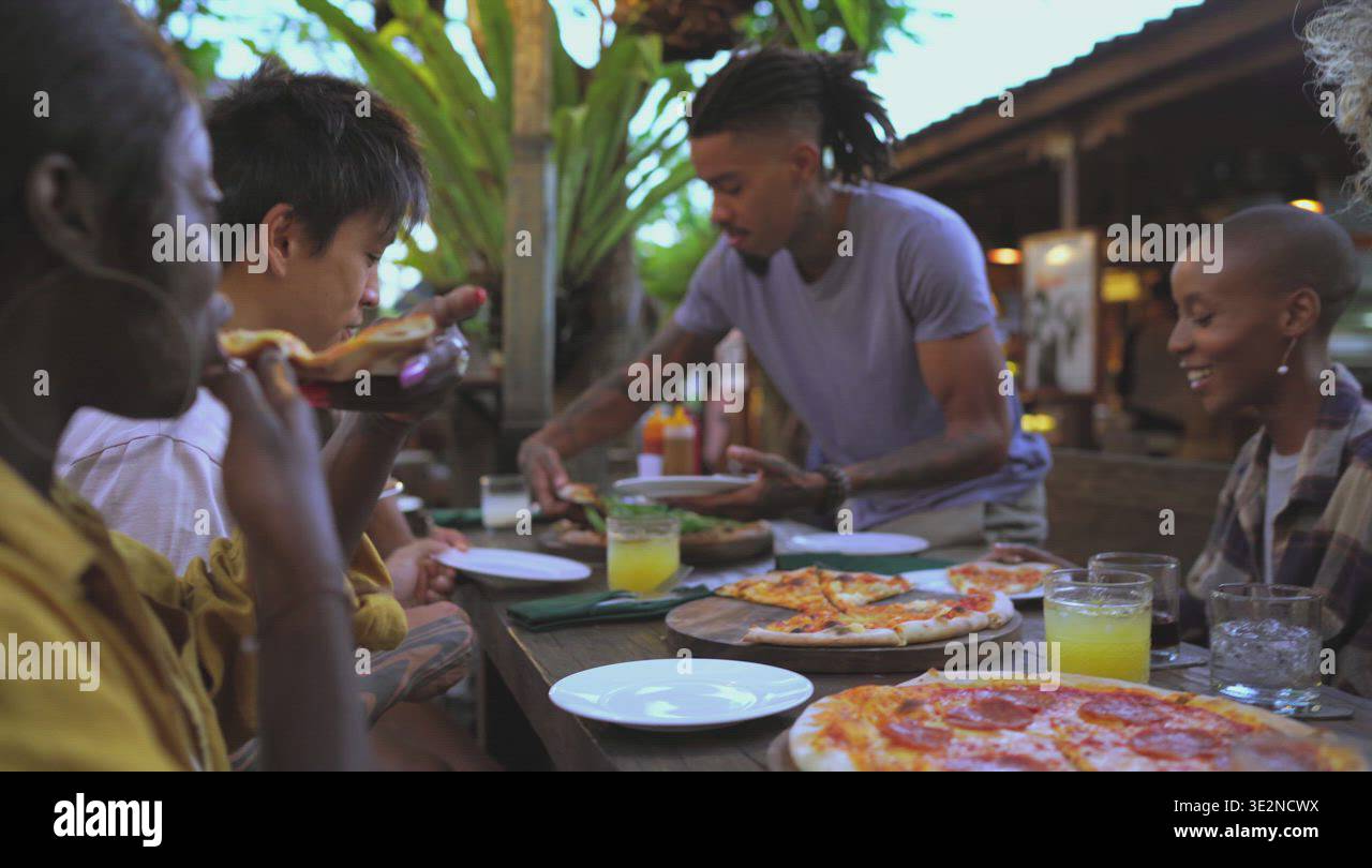 Friends serving pizza slices to each other while enjoying dinner Stock ...