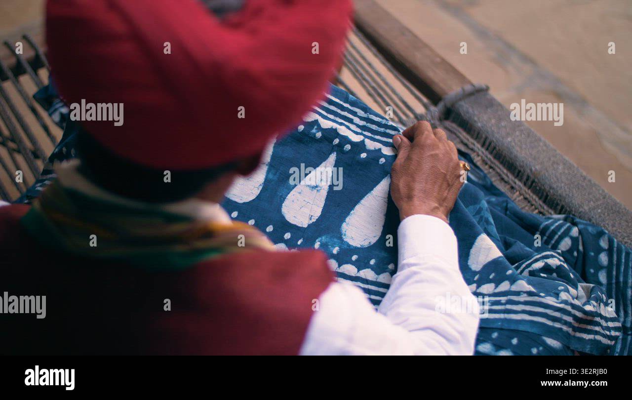 Over the shoulder scene of an Indian man with turban stroking a cloth ...