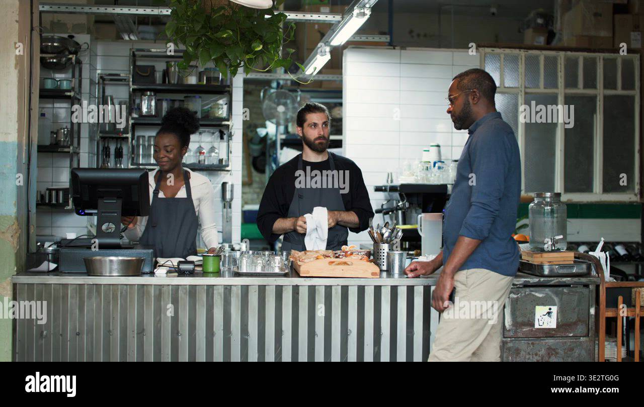Waiter showing baking to cafe owner near waitress writing in notebook ...
