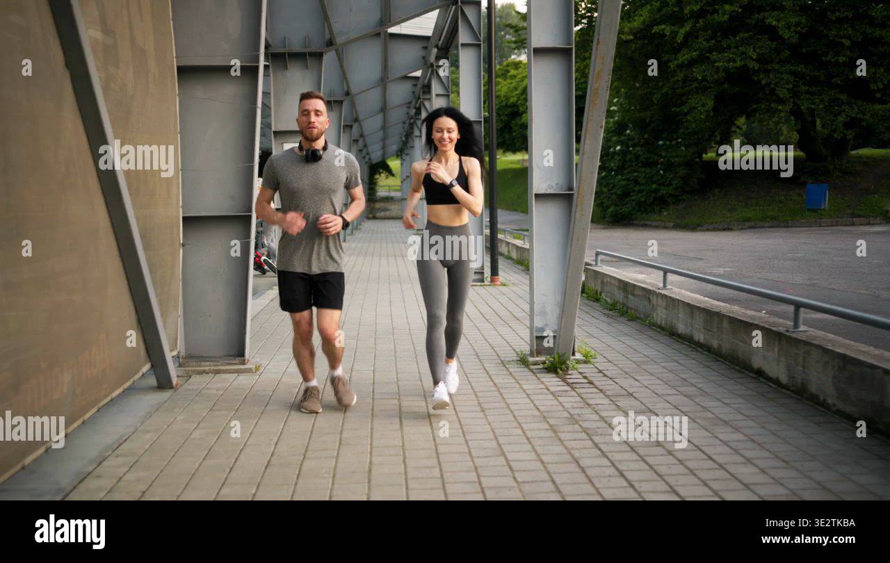 Athletic couple with smartwatches on wrists jogging in stadium walkway ...
