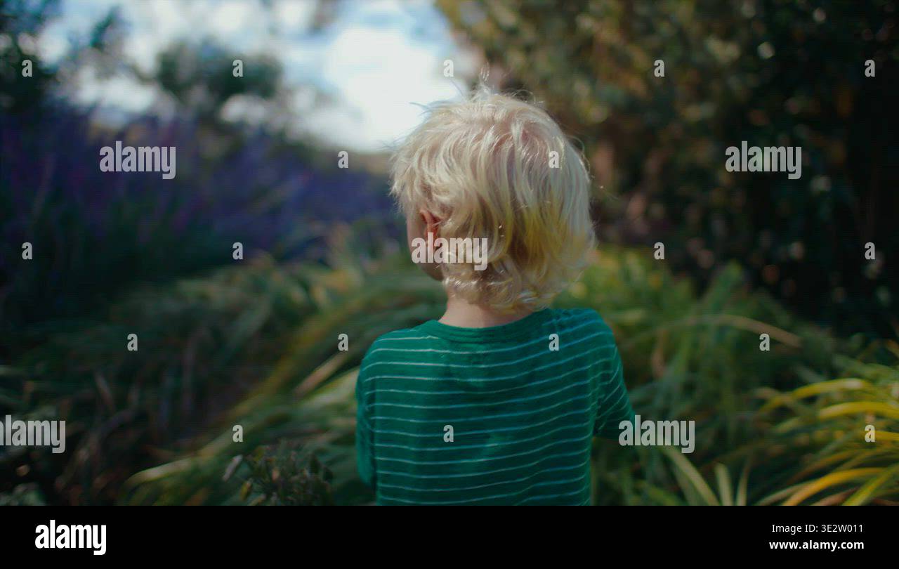 Young blonde child holding a magnifying glass up to their eye outside ...