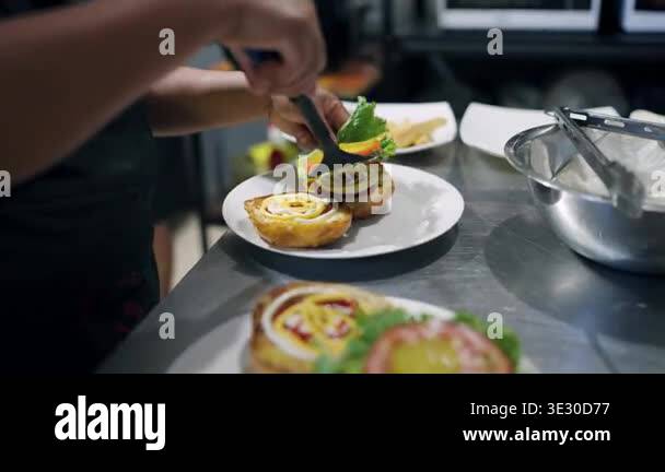 Professional cook assembling a fresh burger with lettuce, tomato, and ...
